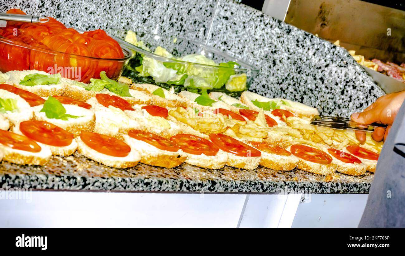 Lettuce and tomato plates on worktop, opened burgers in a row with ...