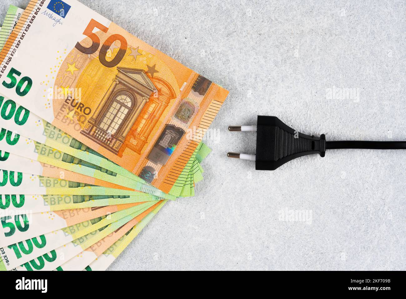 Black electic cable and plug with many euro banknotes over light ...
