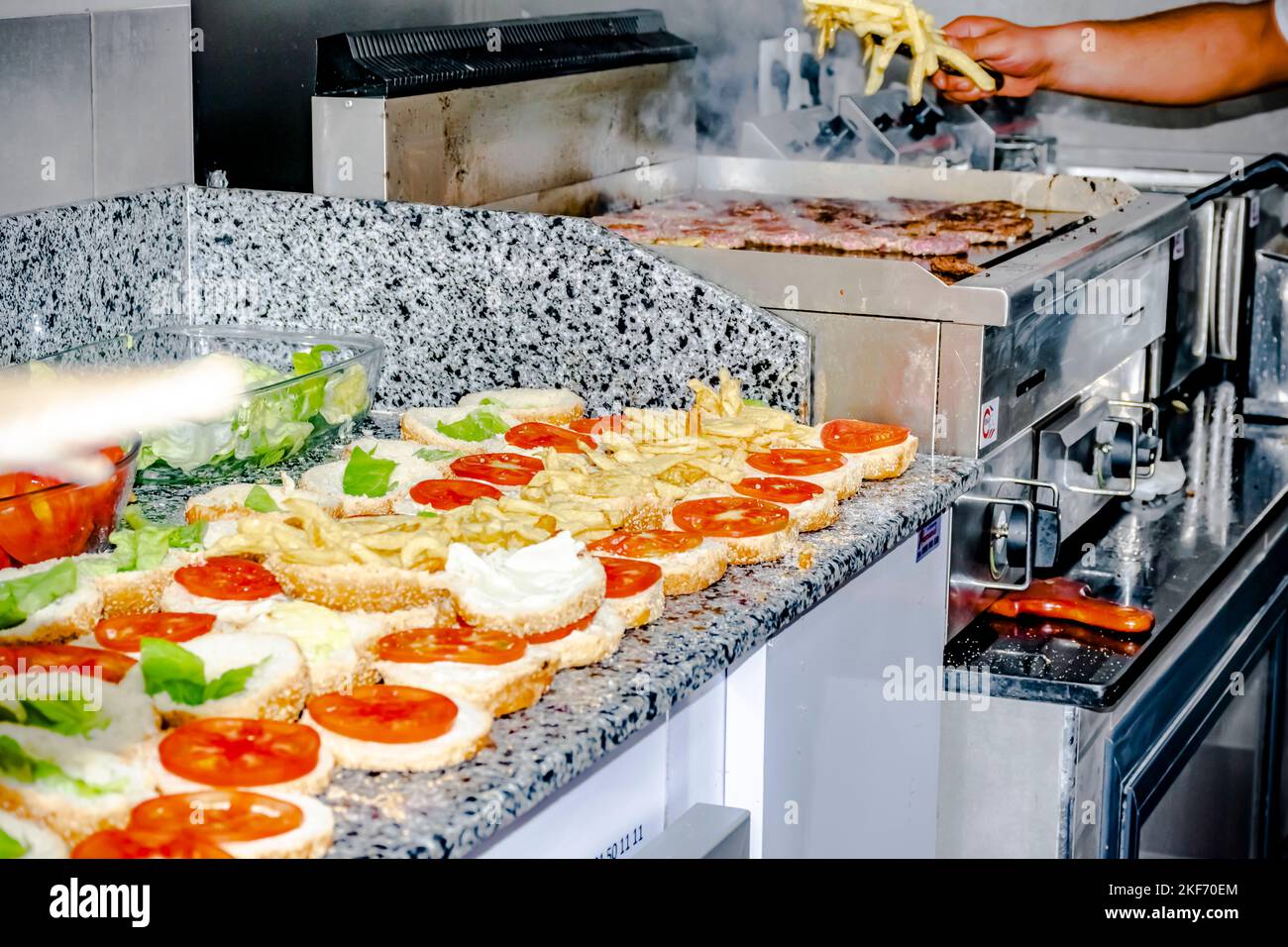 opened burgers on worktop with french fries, lettuce and tomato. Cooker ...