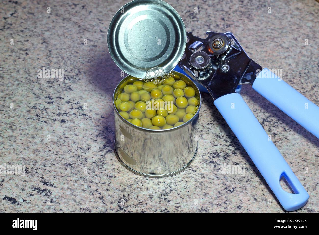 Tin of peas opened and a tin opener next to it Stock Photo - Alamy