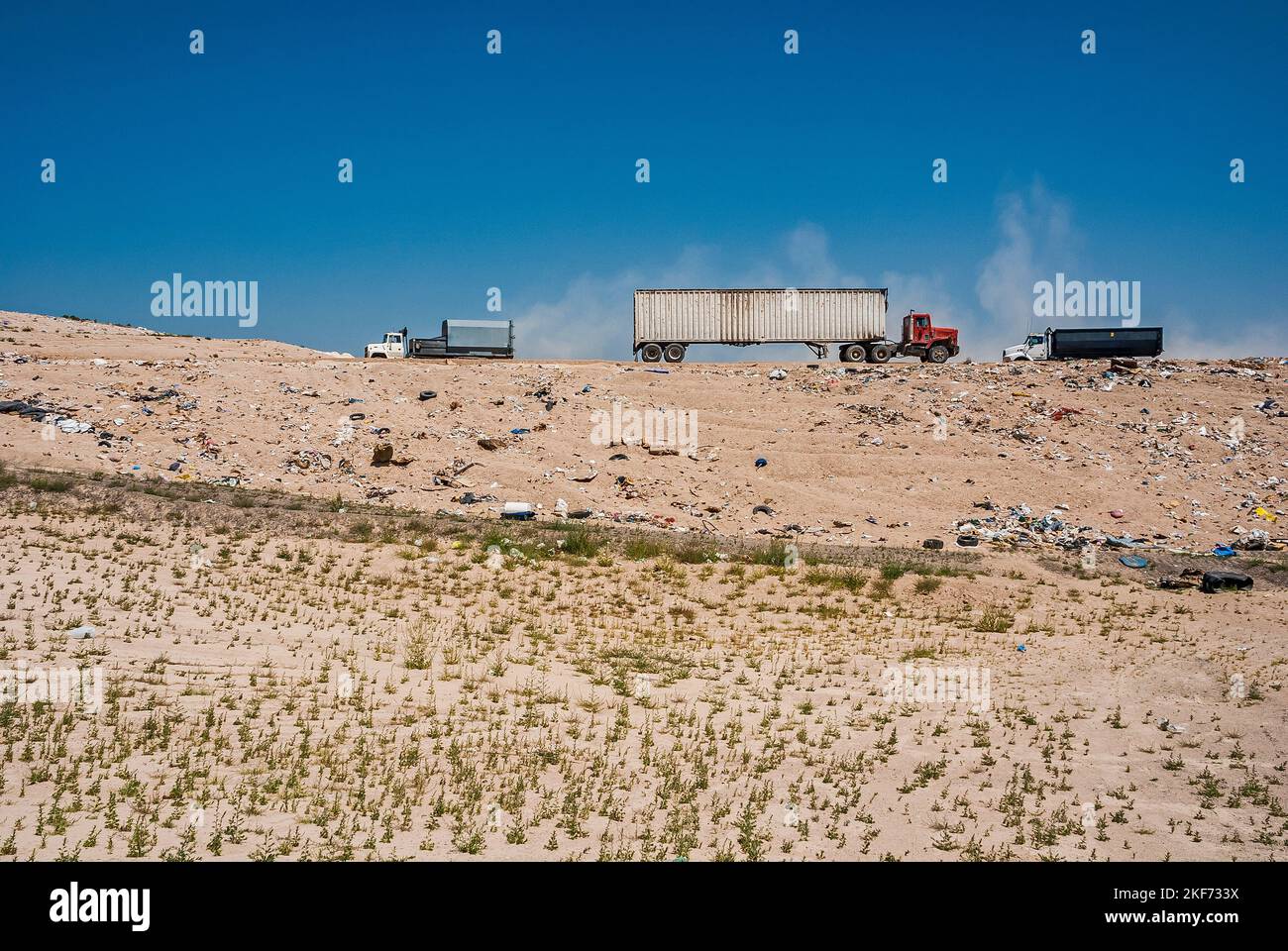 Three trucks raise dust on the top of a hill at an active landfill ...