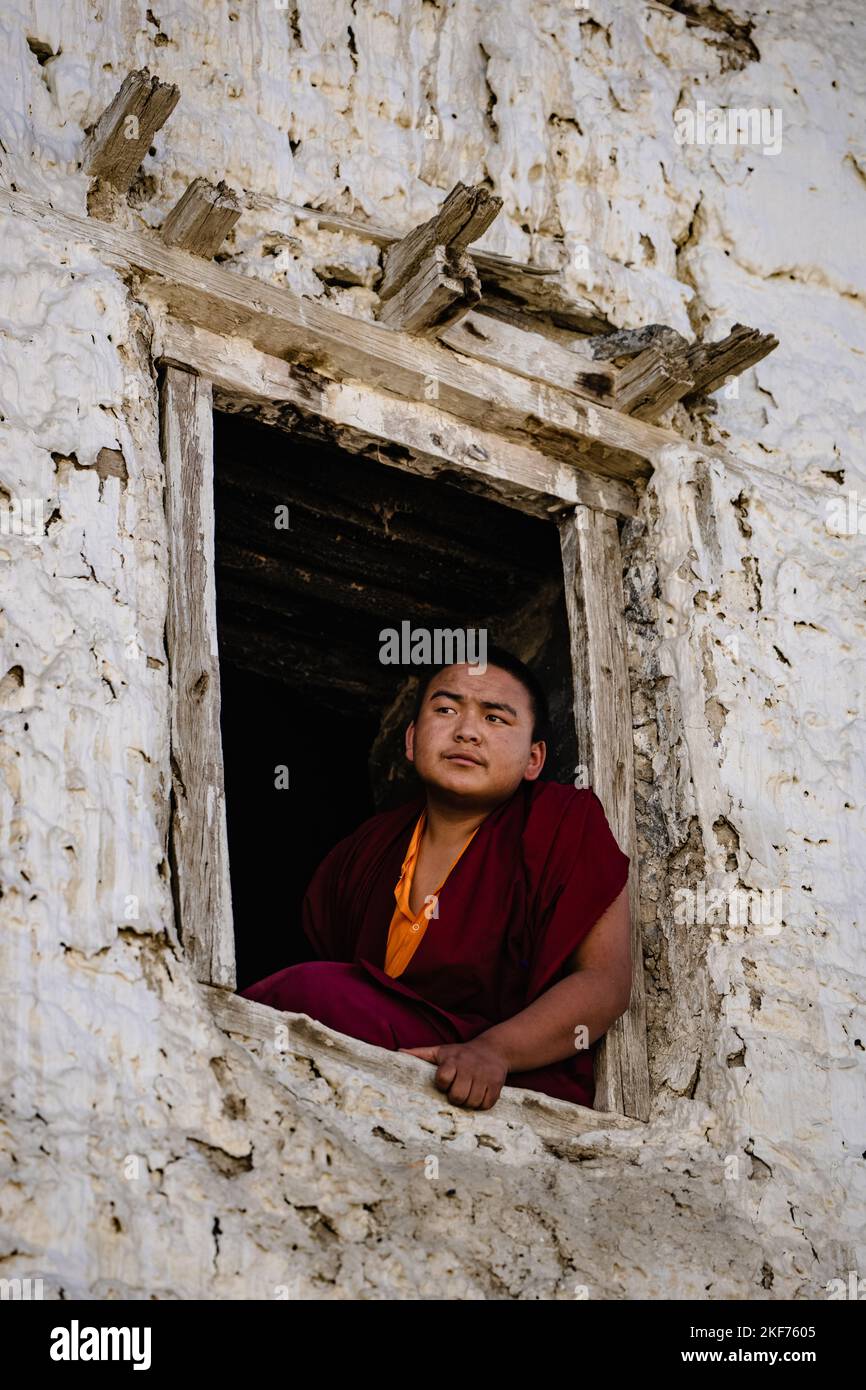 A young Tibetan Buddhist Monk sitting by the window of old building and ...