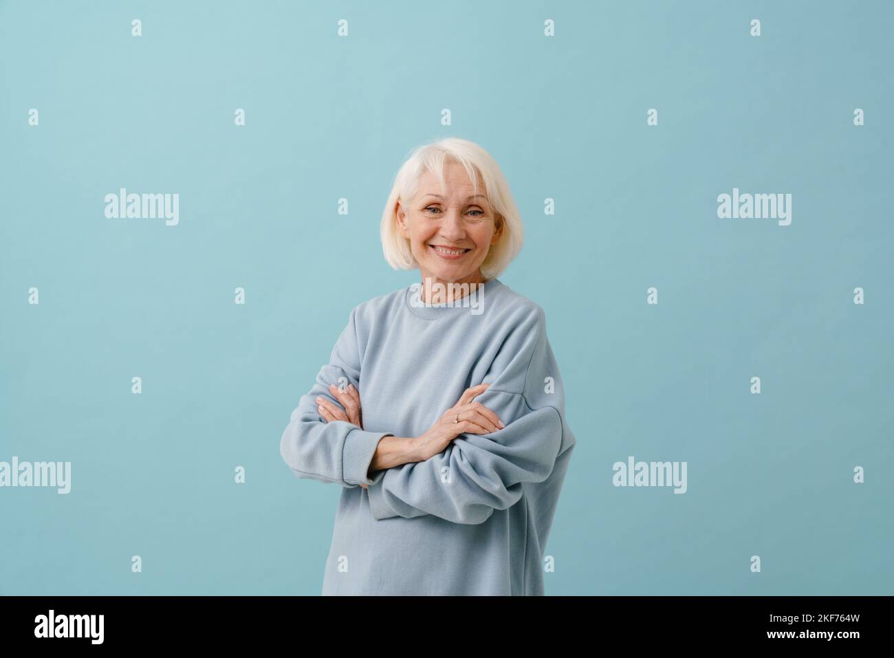 Beautiful smiling senior woman in blue pullover standing with folded ...