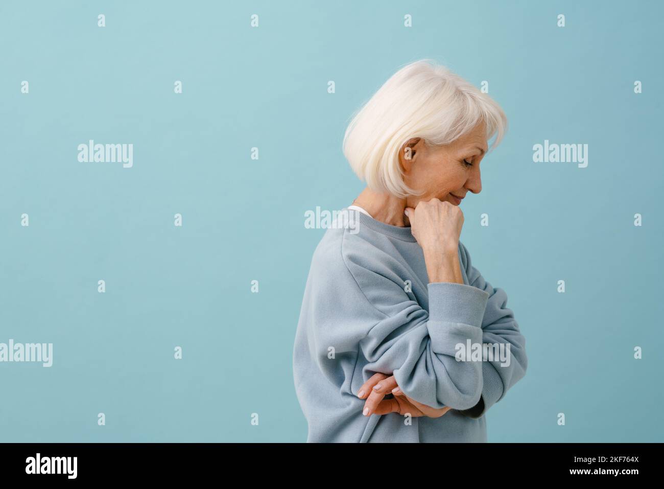 Beautiful pensive senior woman in blue pullover looking downward over ...