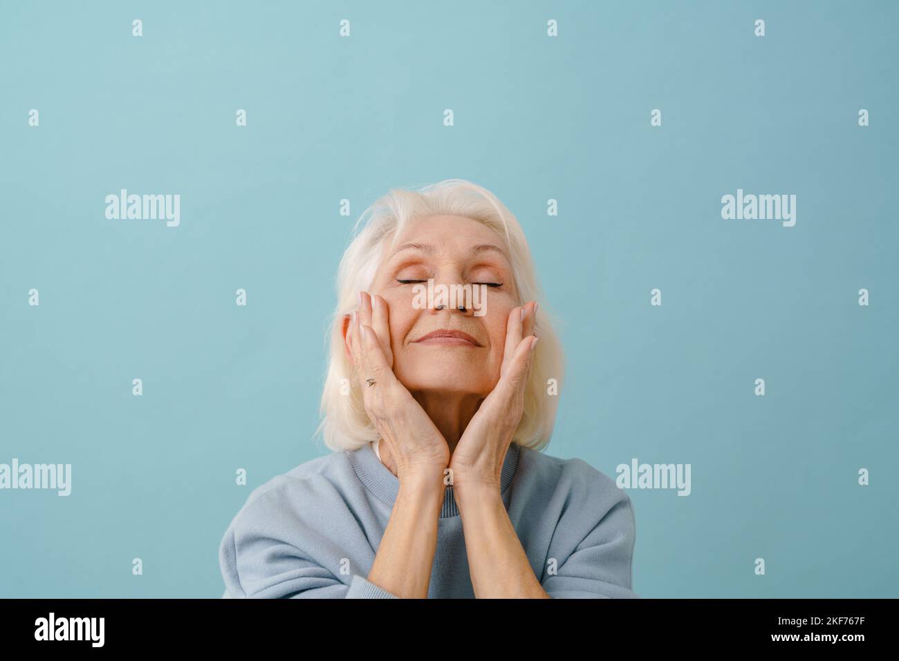 Beautiful smiling senior woman in blue pullover with closed eyes ...