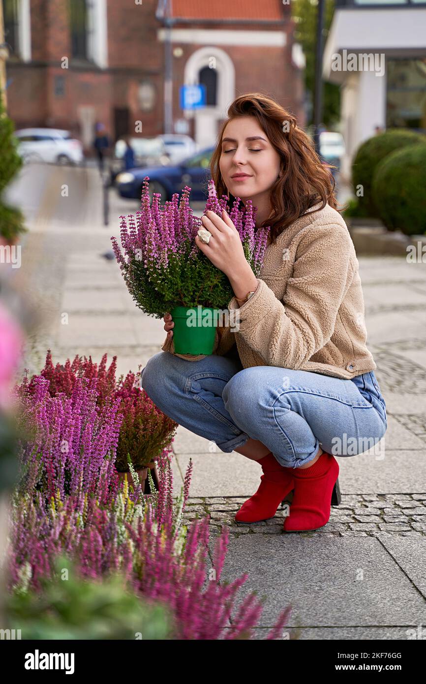 Young beautiful woman holding a pot with blooming violet heather plant ...
