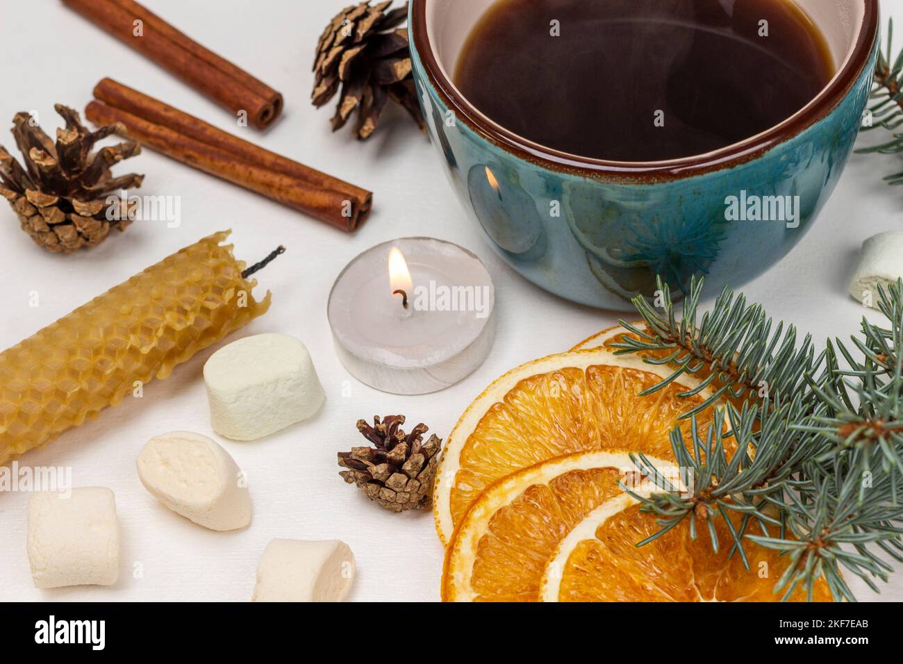 A mug of coffee, a lit candle, a spruce branch, cones and dry orange ...