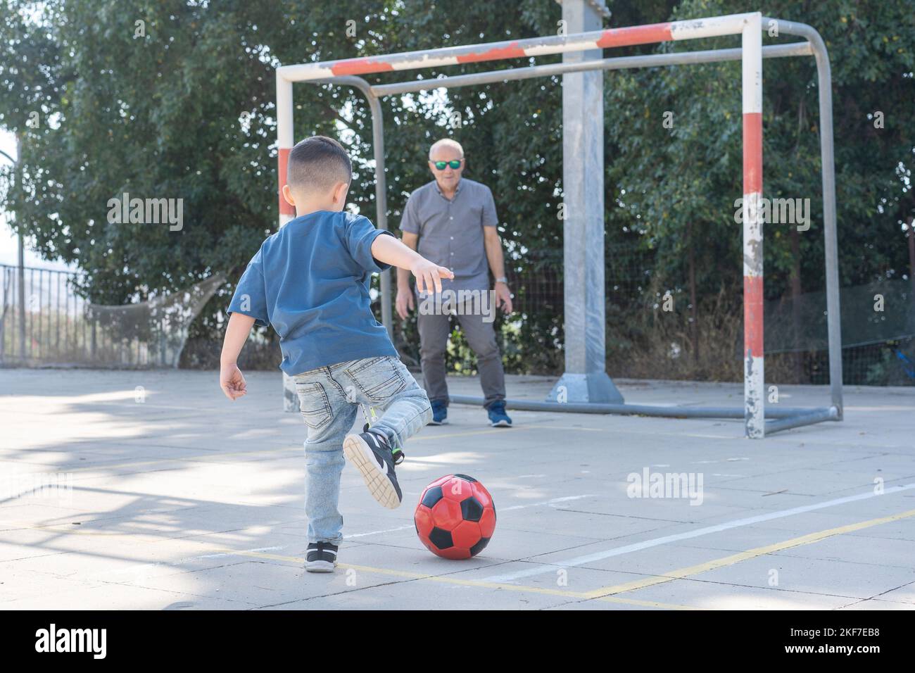 Back view of child kicking soccer ball. Grandfather soccer goalkeeper ...