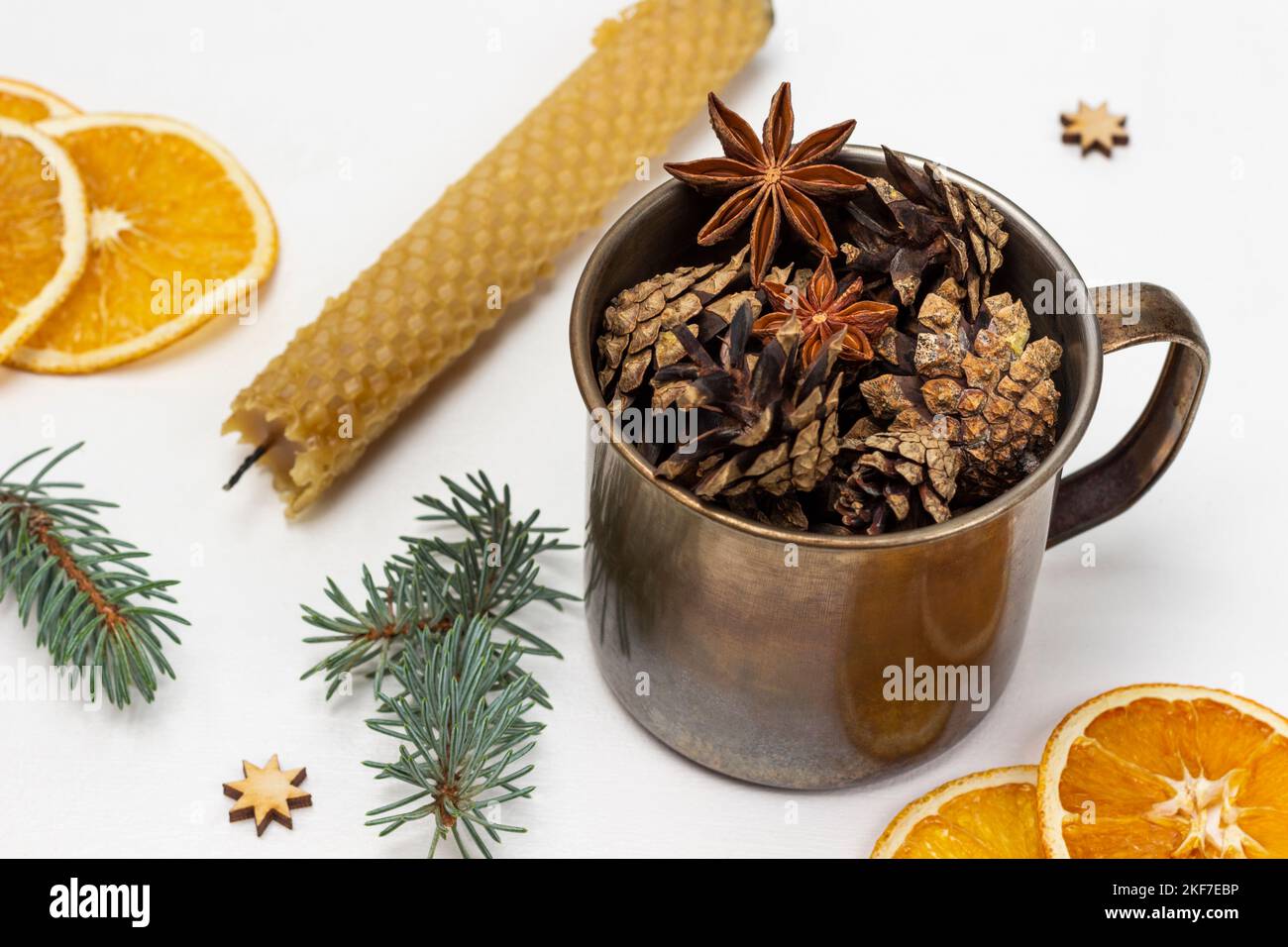 Cones in a metal mug, a candle, sprigs of spruce and dry orange slices ...