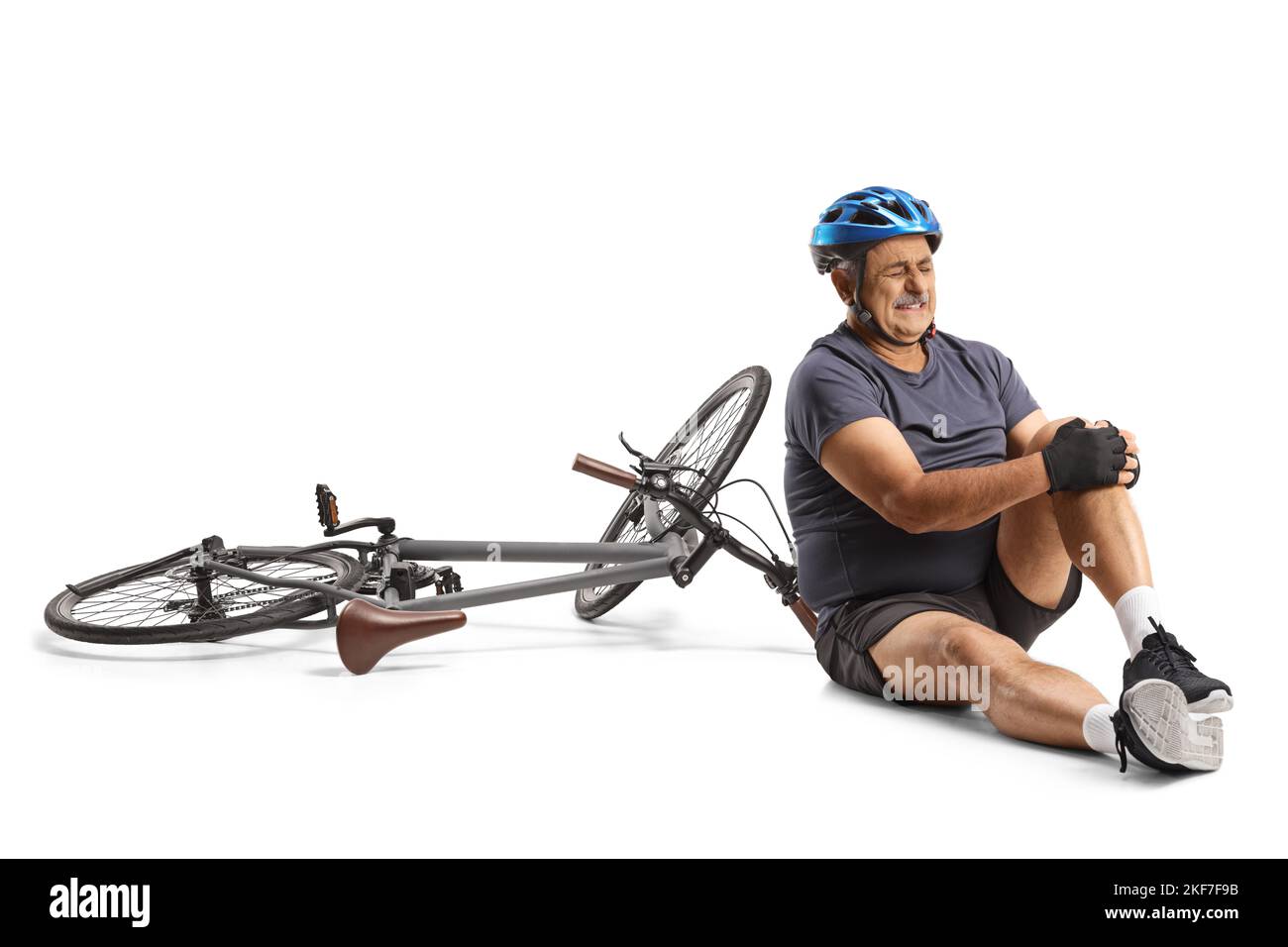Mature male bicycle rider sitting on the ground and holding his knee ...