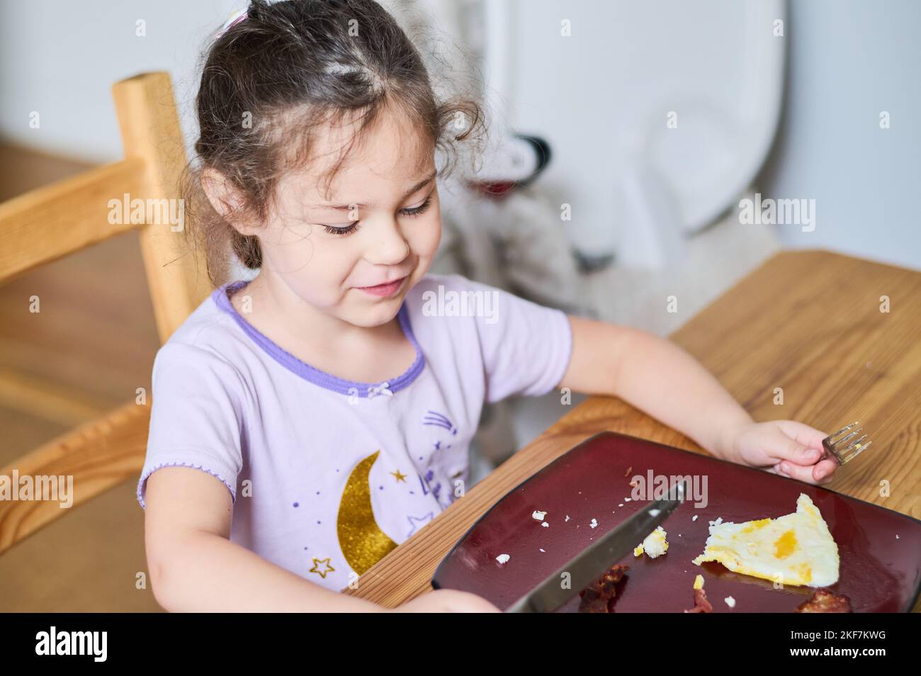 Young girl eating eggs and bacon with knife and fork for the first time ...