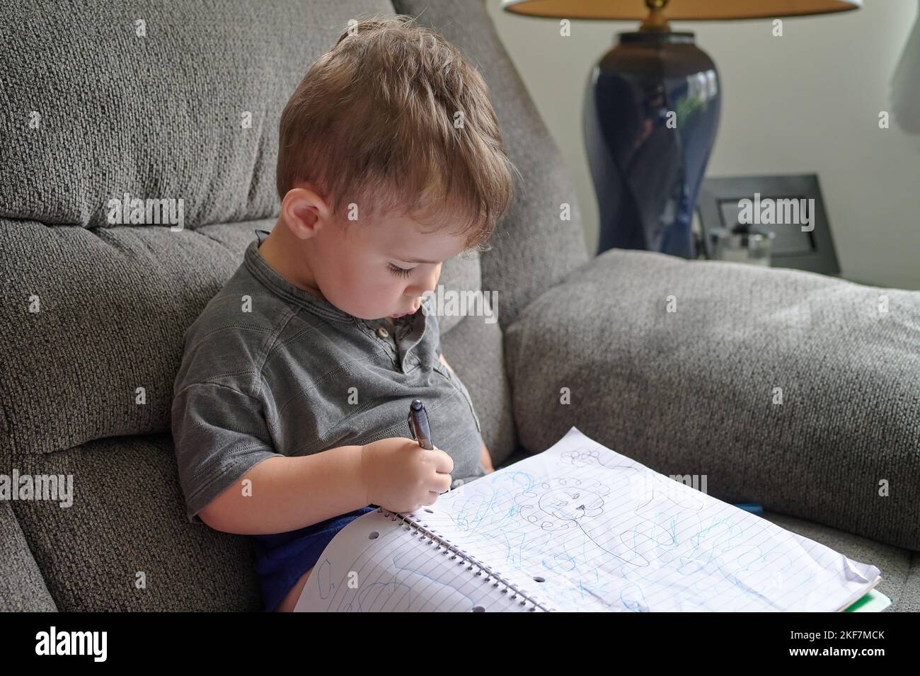 young boy drawing doodles in a notebook while sitting on a couch at ...