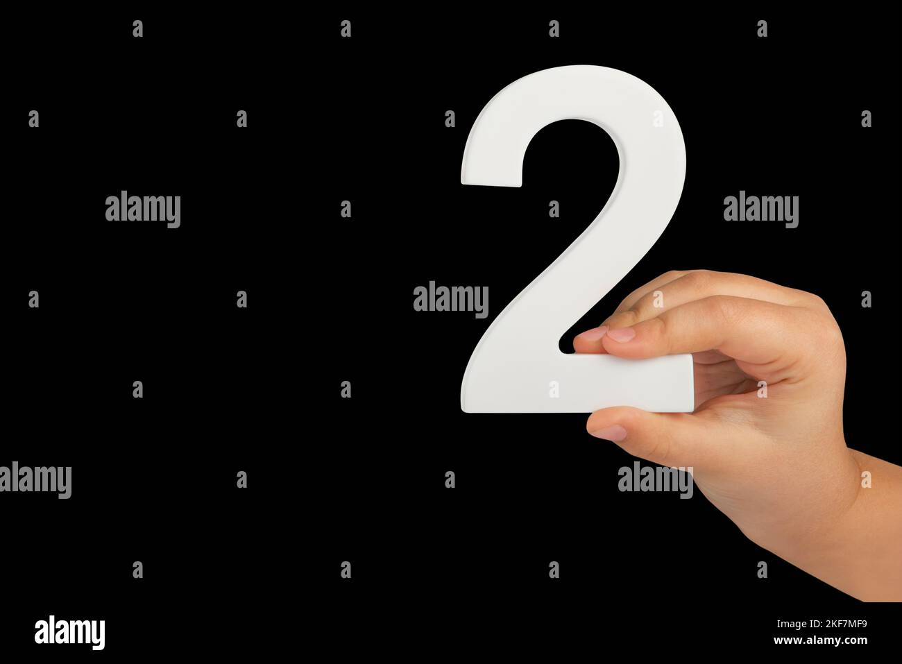 Close-up hand holding a white number 2 on a black background. Number ...