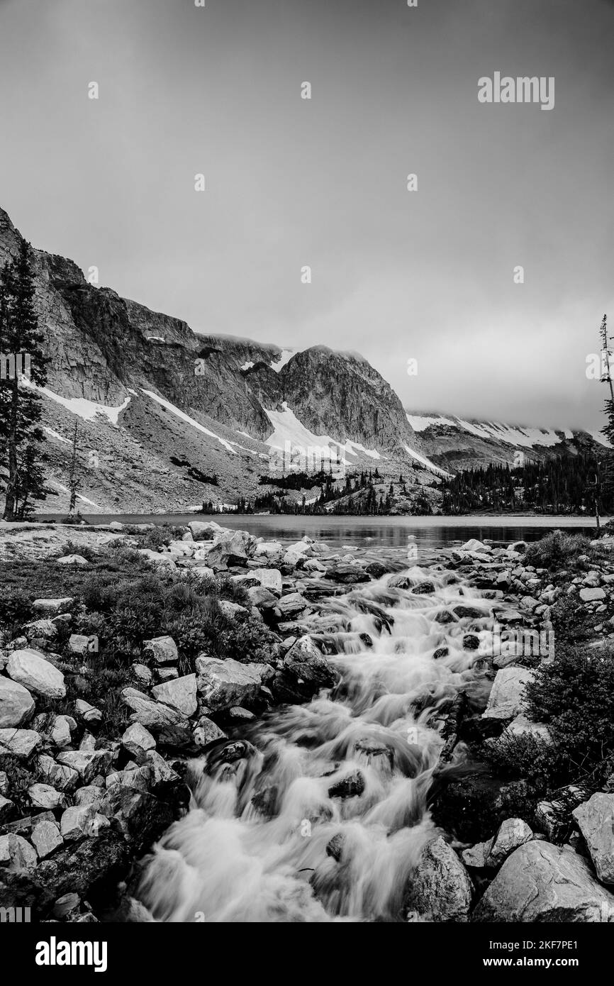 A vertical grayscale of a rocky stream surrounded by hills against a ...