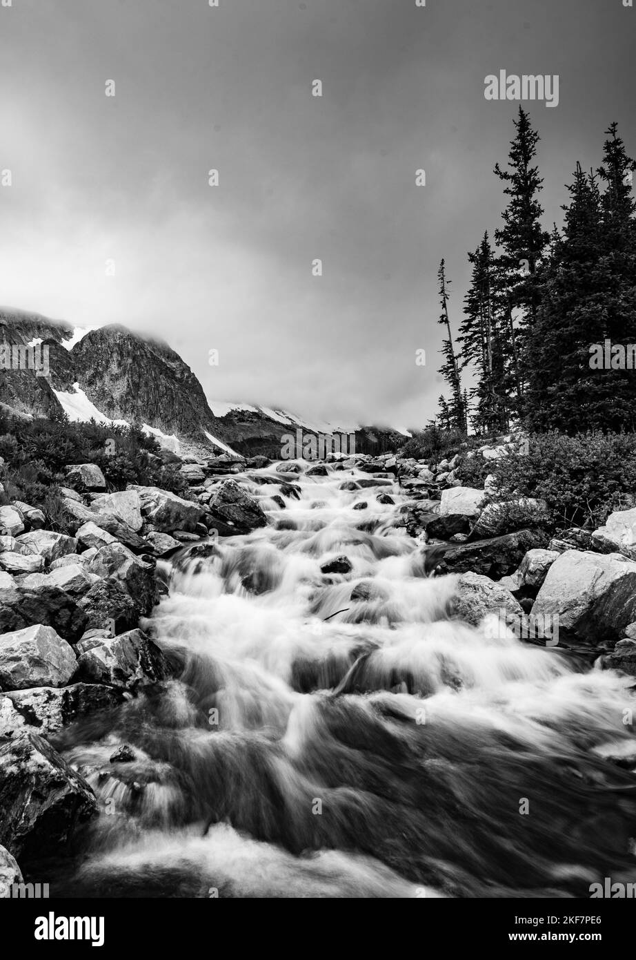 A vertical grayscale of a rocky stream surrounded by hills against a ...