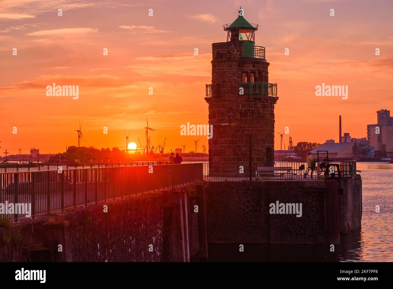 Stone lighthouse on a river harbour under a dramatic sky at sunset ...