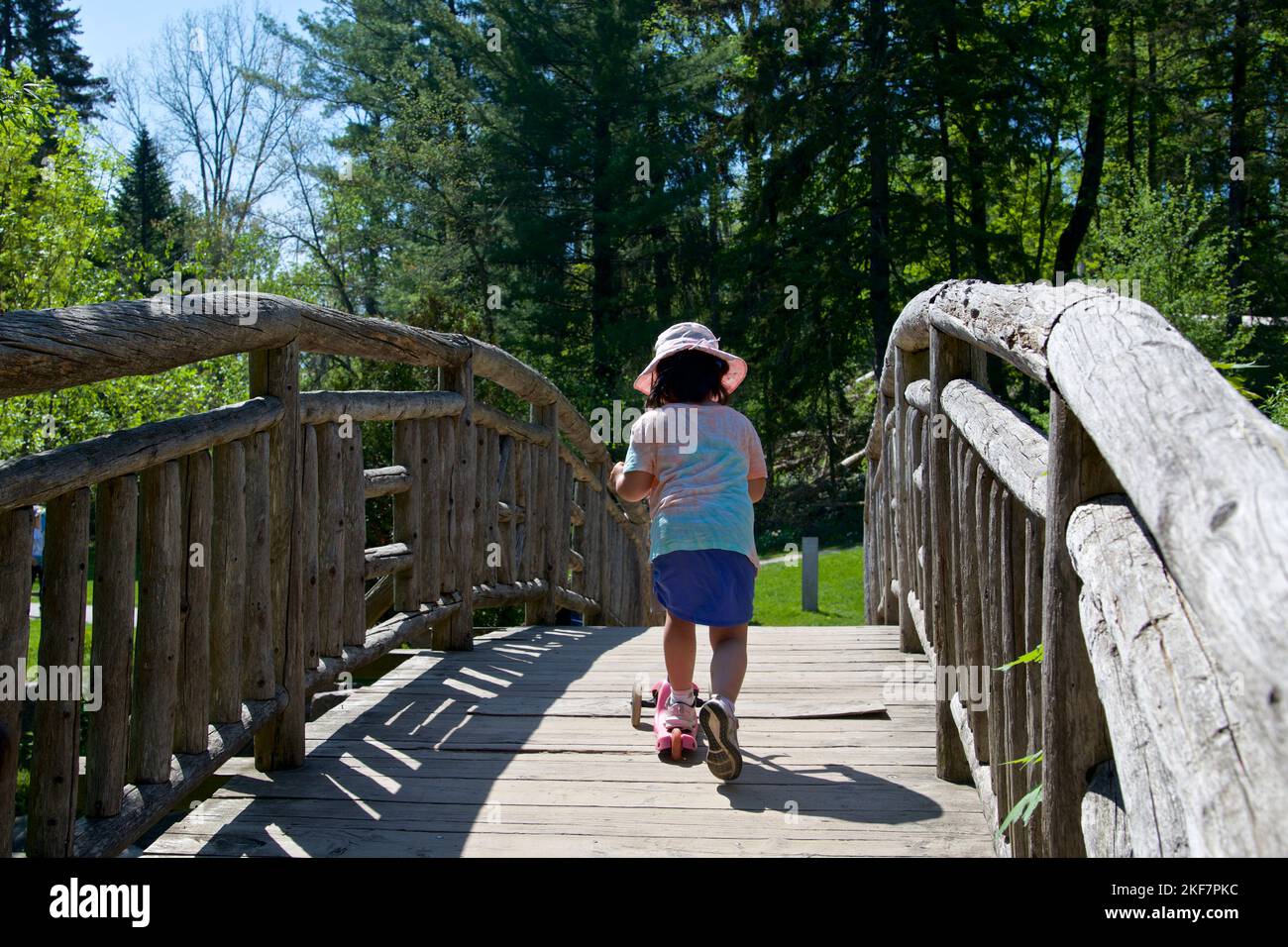 A girl riding a scooter across a bridge in a public park in springtime ...