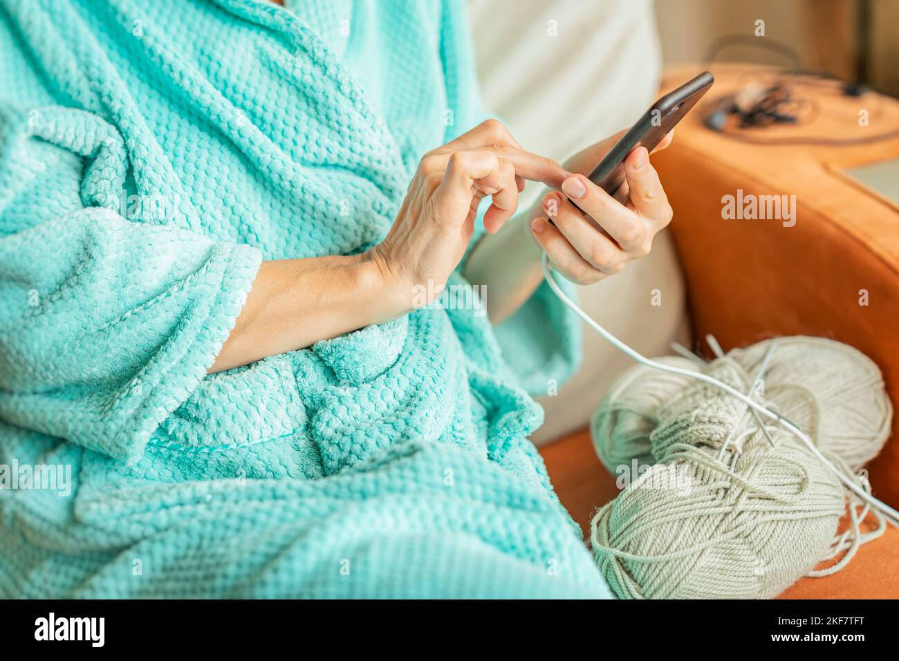 Abstract woman sitting on sofa at home, using smartphone, knitting ...