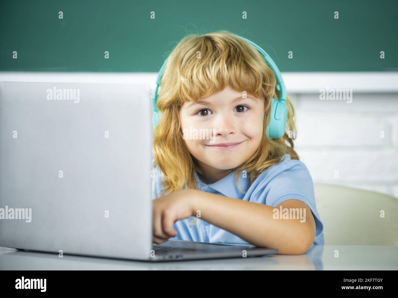 Funny school kid boy with laptop computer and headphones in class at ...