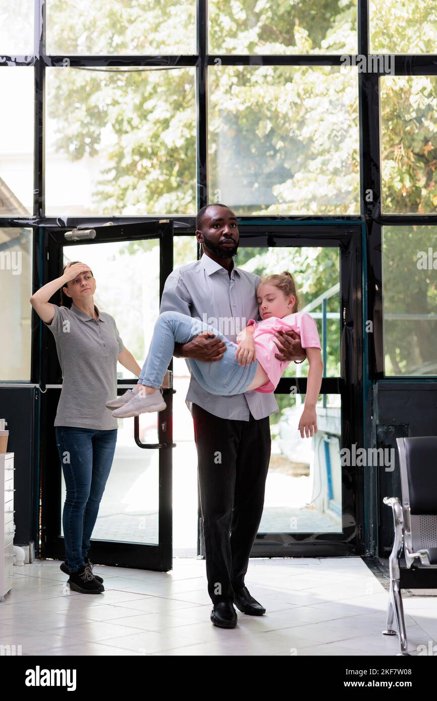 Scared dad walking in hospital waiting area holding fainted unconscious ...