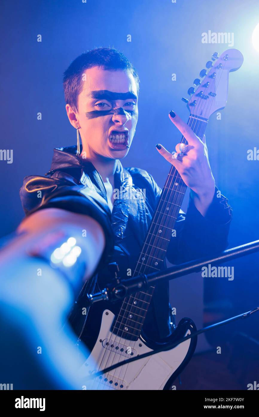 Playful guitarist showing rock sign on camera and playing guitar ...