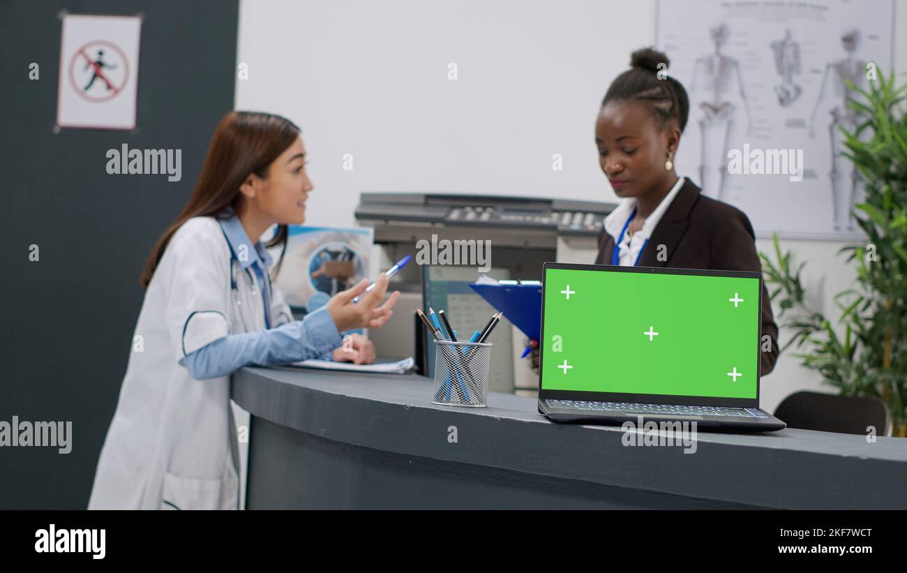 Diverse medical team working with greenscreen on laptop at reception ...
