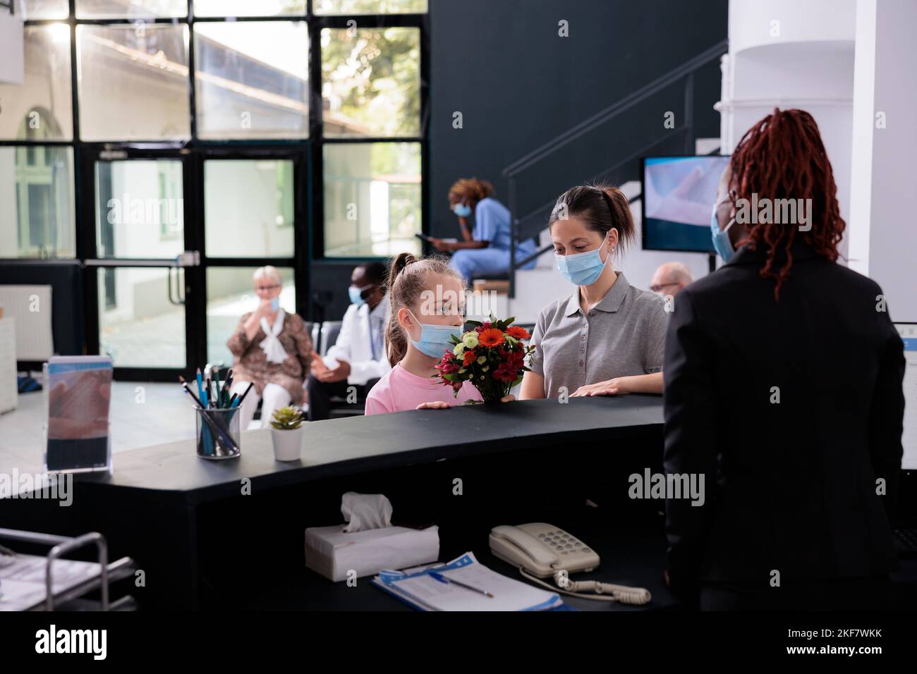 Mother standing at reception counter with child discussing with ...