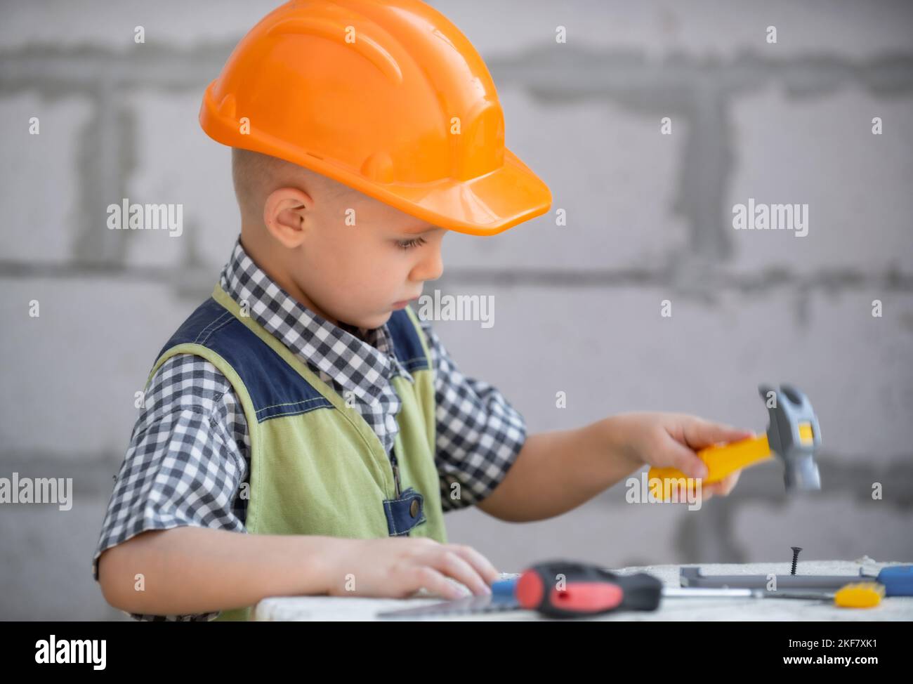 Kid in hard hat holding hammer. Little child helping with toy tools on ...