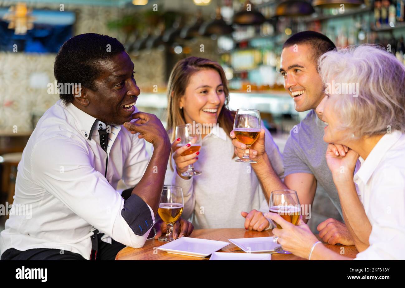 Company of multiracial friends drinking beer and talking with each ...
