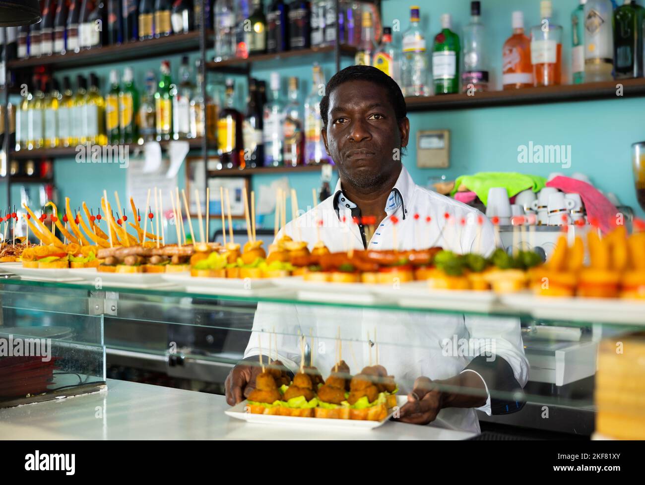 Serious African American bartender standing with plates of pinchos in ...