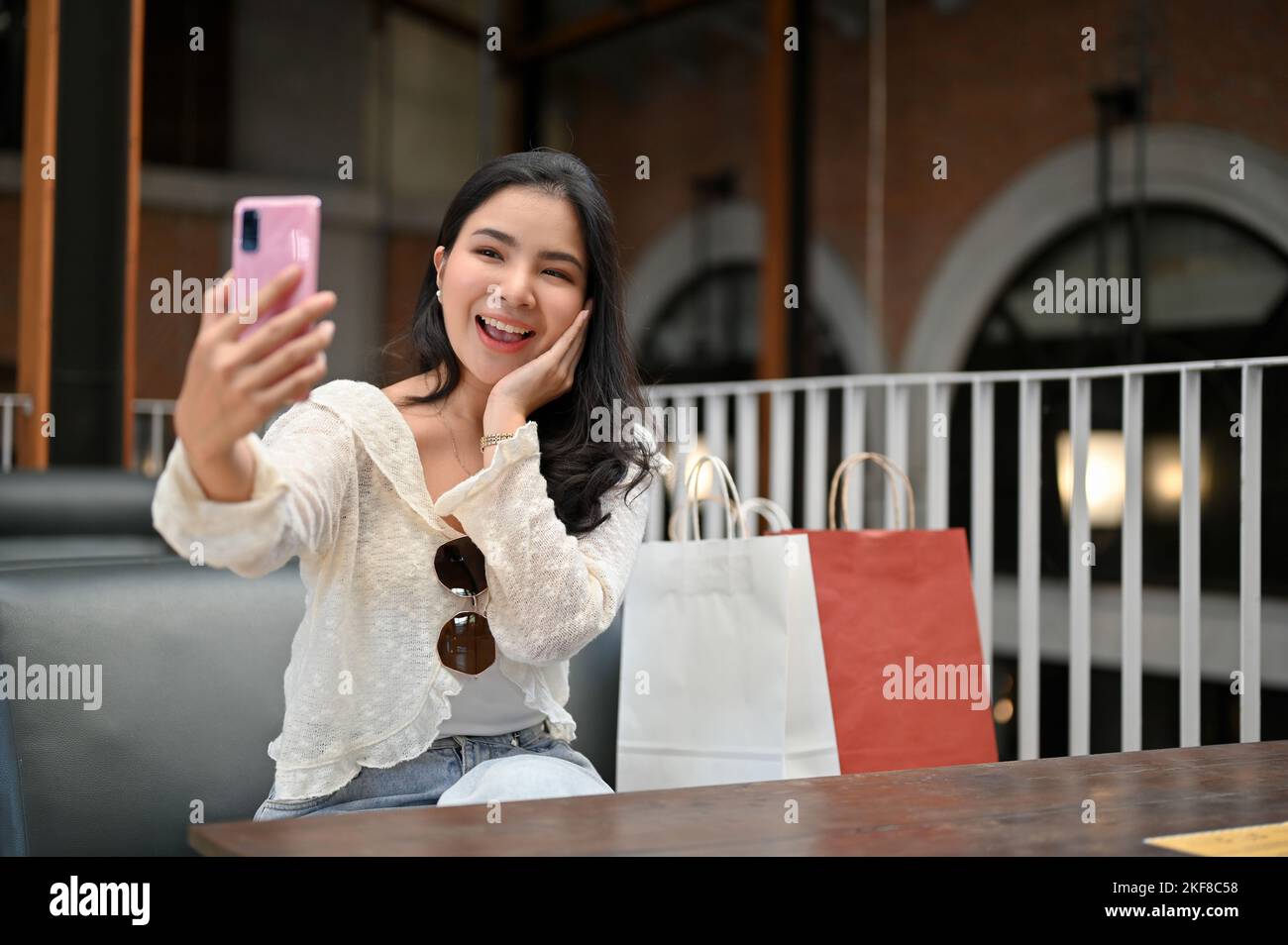 Charming and happy young Asian woman with her shopping bags, using her ...