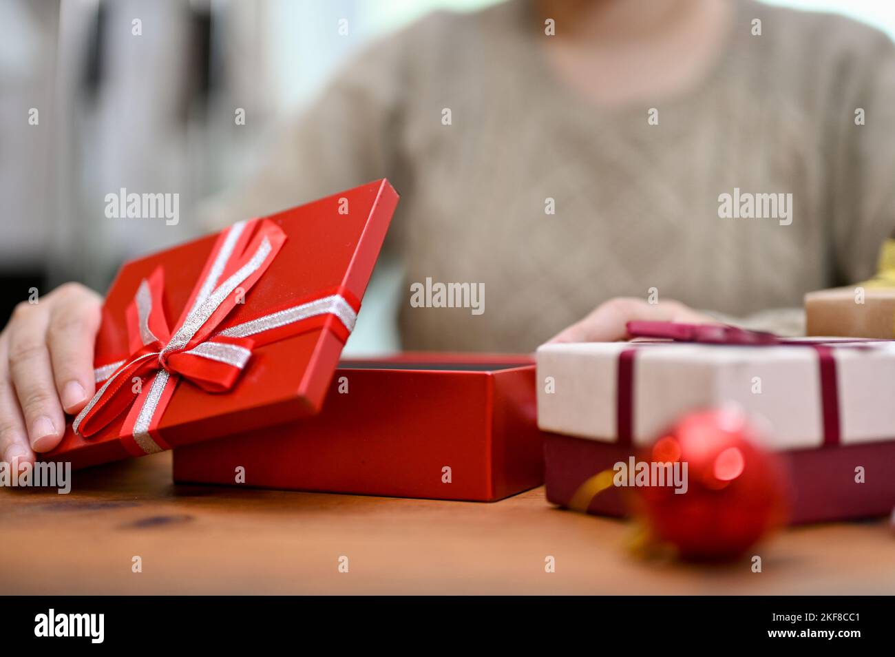 A woman open a Christmas gift box at her table. A female packing her ...