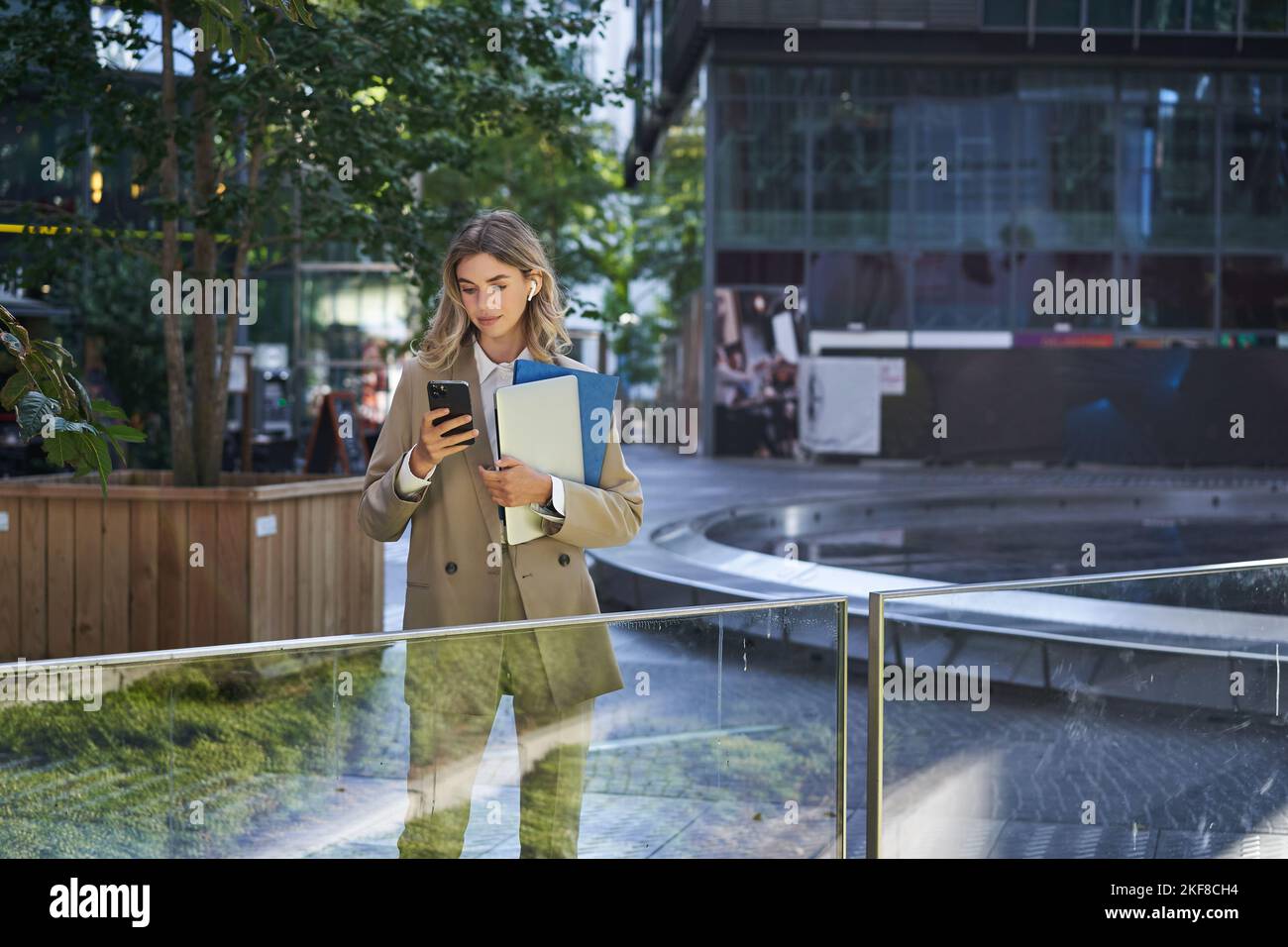 Portrait of corporate woman in suit using mobile phone, waiting for ...