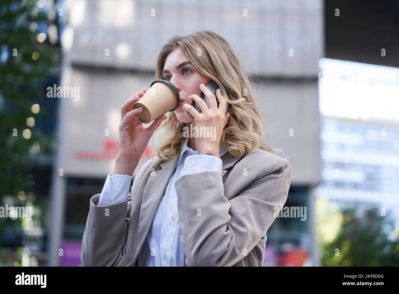 Businesswoman walking in city centre, drinking coffee and talking on ...
