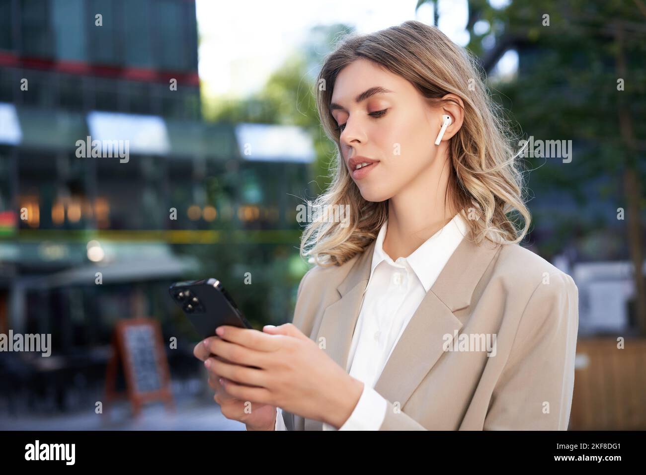 Successful businesswoman in beige suit, wireless headphones, looking at ...