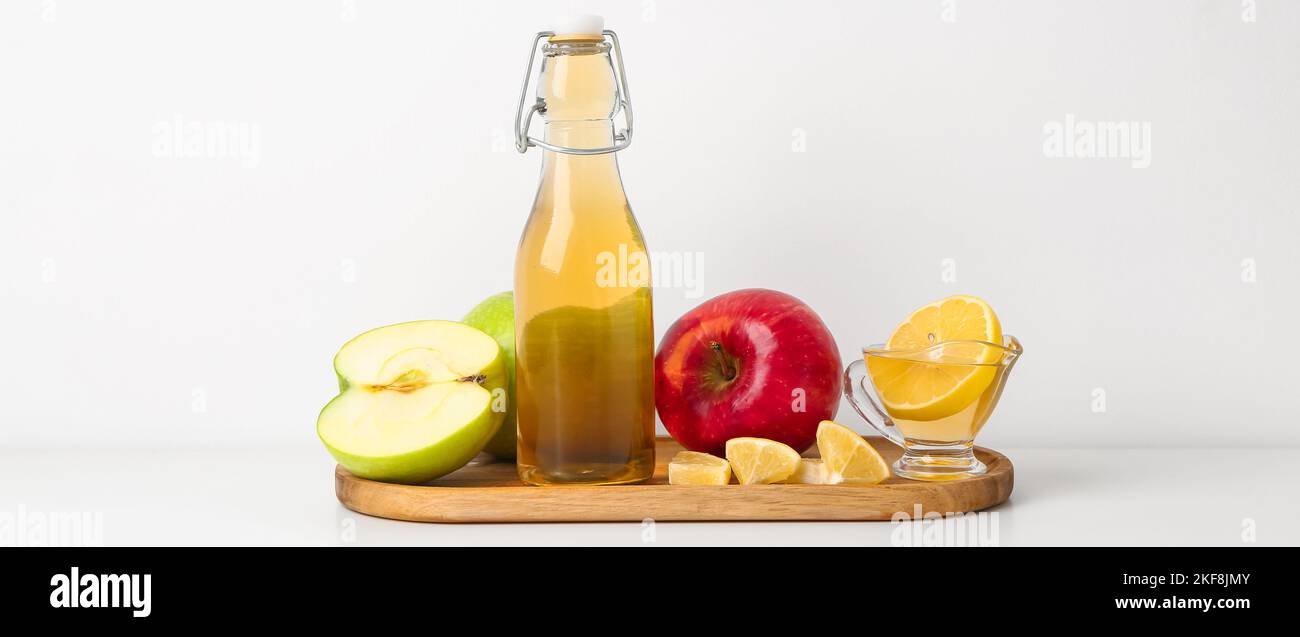 Bottle of apple cider vinegar and fresh fruits on light background ...