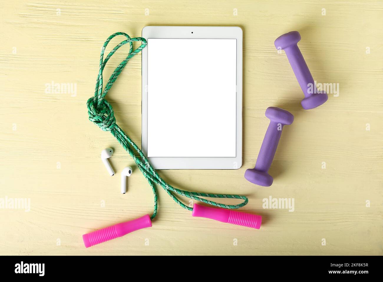 Tablet computer with earphones, skipping rope and dumbbells on yellow ...