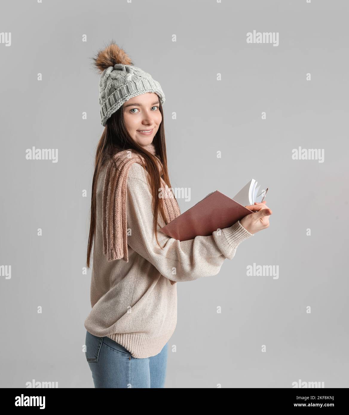 Young woman in warm hat reading book on grey background Stock Photo - Alamy