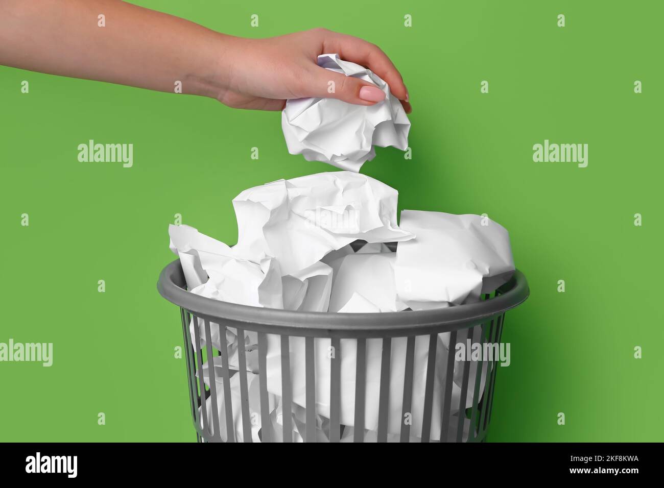 Woman throwing crumpled paper into rubbish bin on green background ...