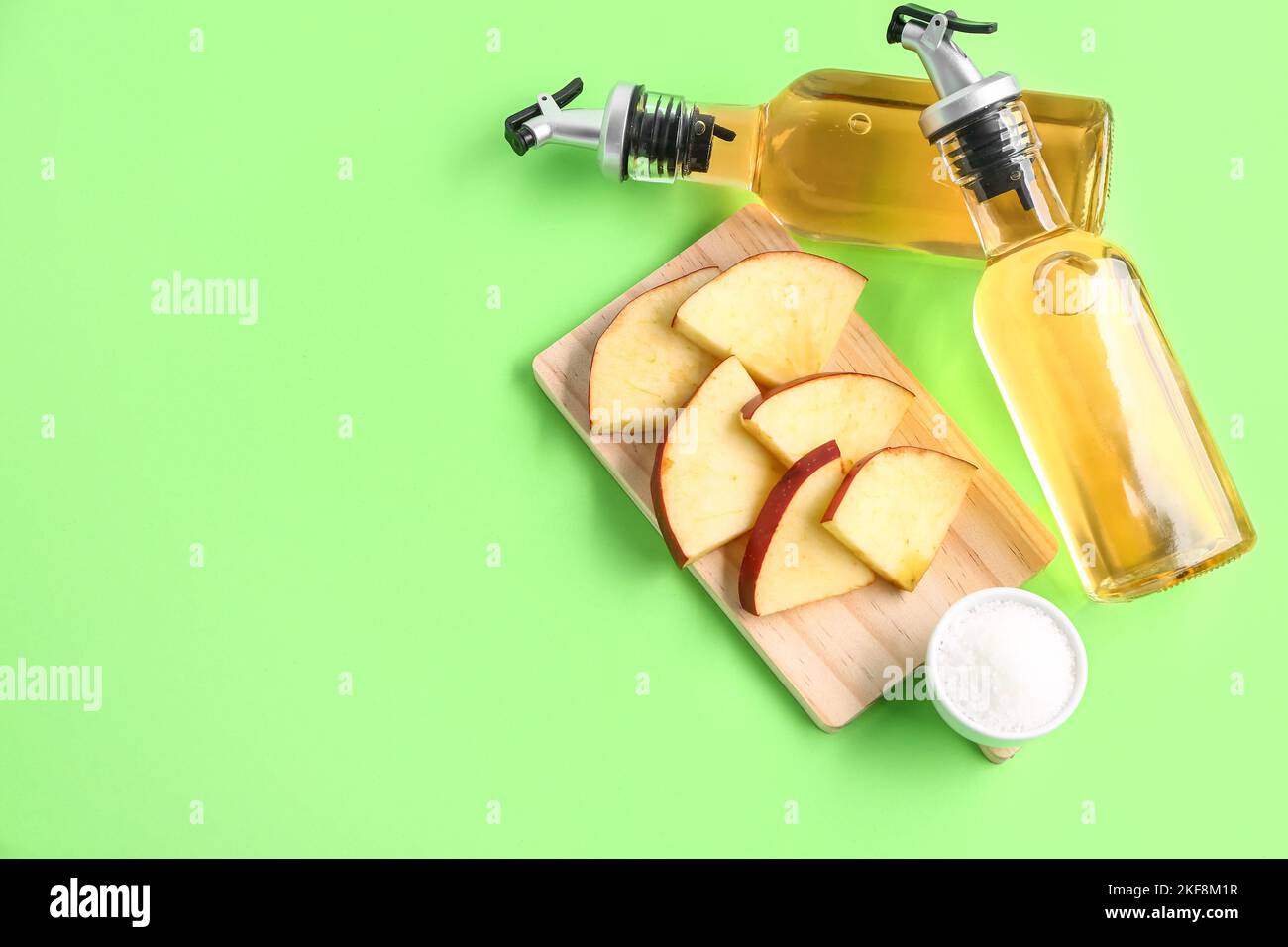 Bottles of apple cider vinegar, wooden board with cut fruits and salt ...