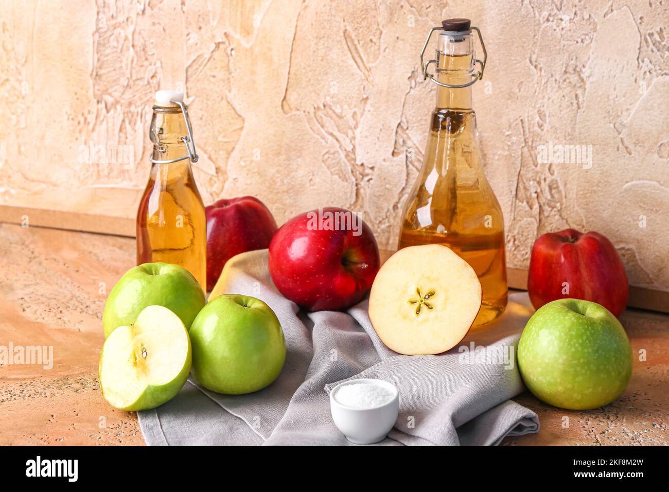 Bottles of apple cider vinegar, fresh fruits and salt on color table ...