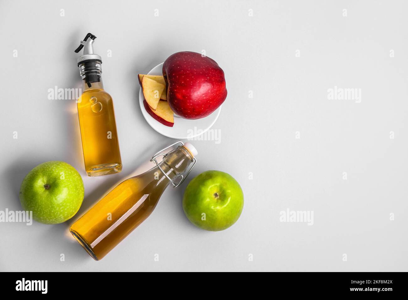 Bottles of apple cider vinegar and fresh fruits on light background ...