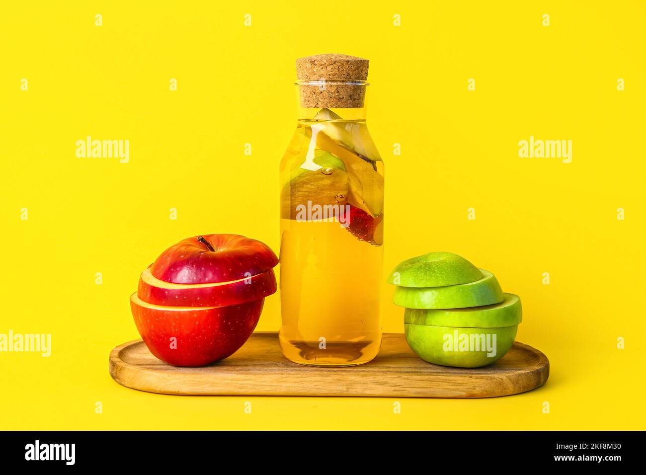 Wooden board with bottle of apple cider vinegar and fruits on yellow ...