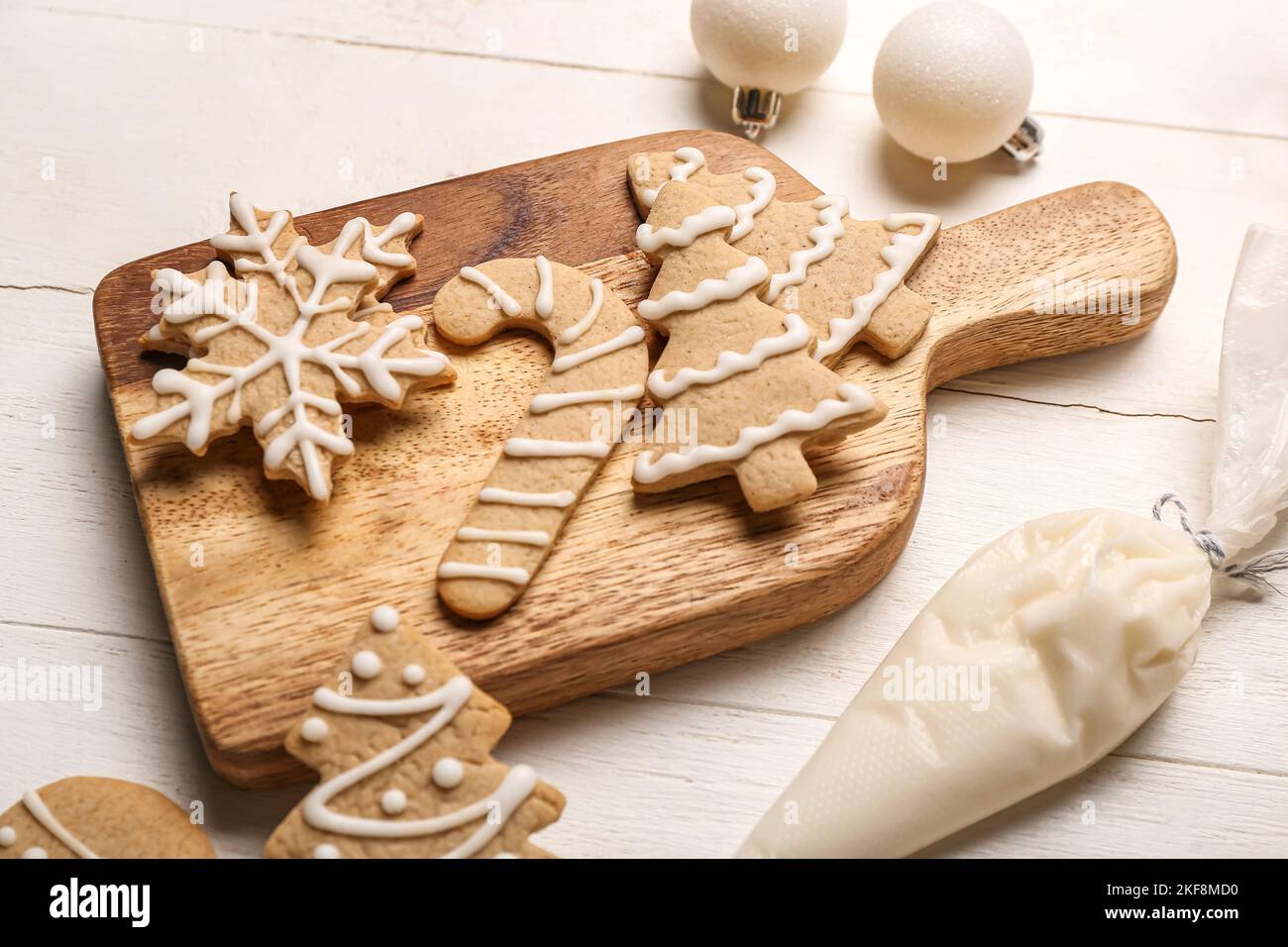 Board of tasty Christmas cookies and bag of cream on light wooden ...