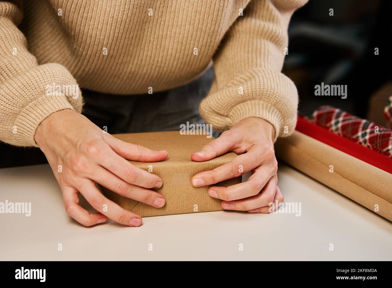 Woman in warm sweater packaging gift box with craft paper. Present for ...