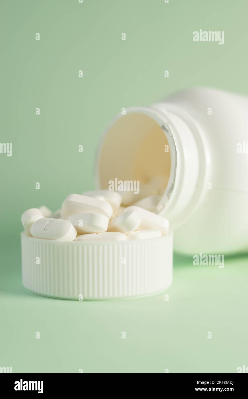 A medicine bottle and a cap filled with pills on green background ...