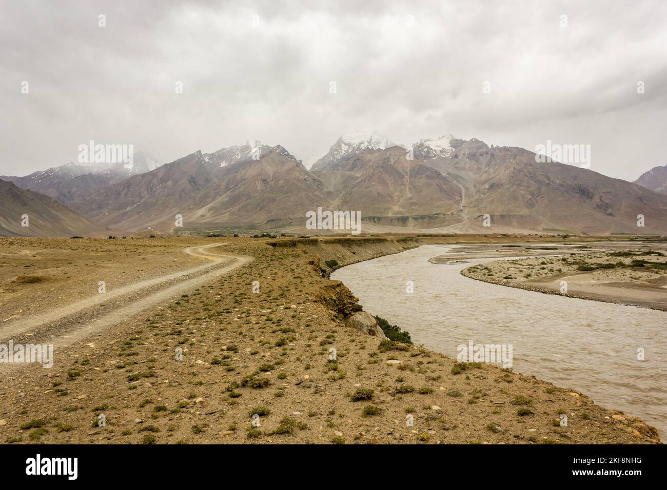 A dirt road along with a winding river in the cold desert landscape of ...