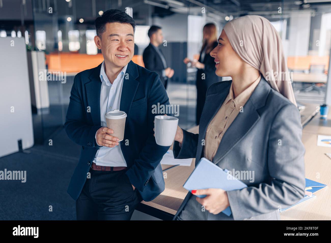 Two happy multiracial colleagues talking and drinking coffee during ...