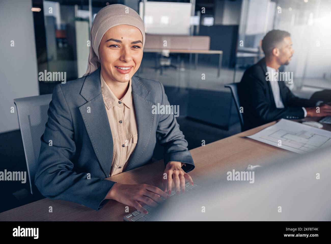 Smiling muslim businesswoman in hijab working on computer while sitting ...