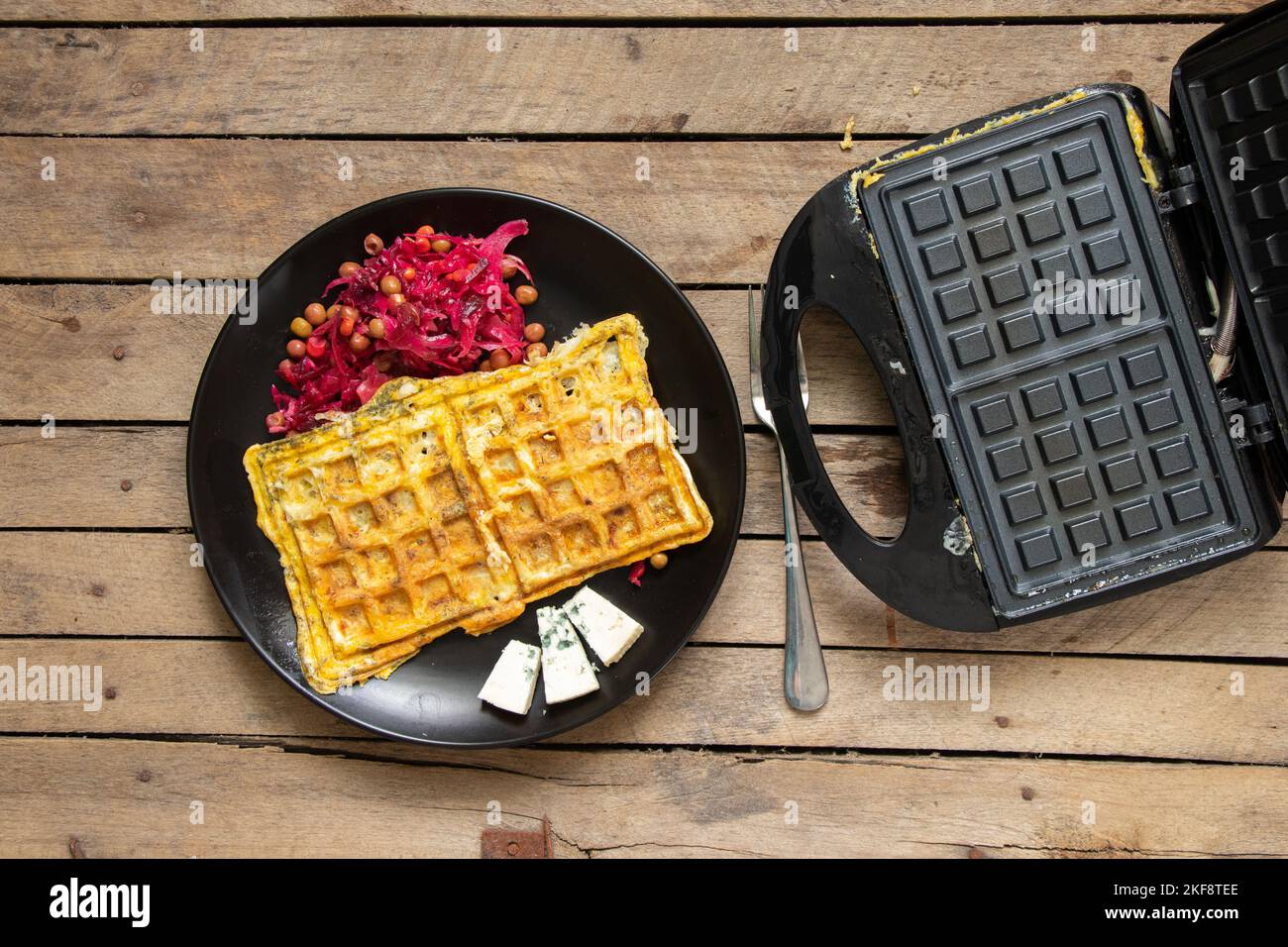 fry scrambled eggs with cheese and spices in a waffle iron on a wooden ...